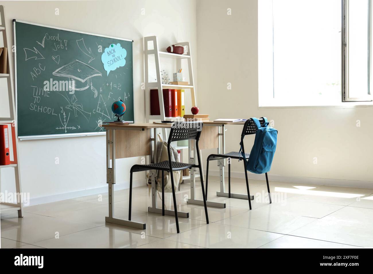 Interior of empty classroom with blackboard, shelf units and desks ...