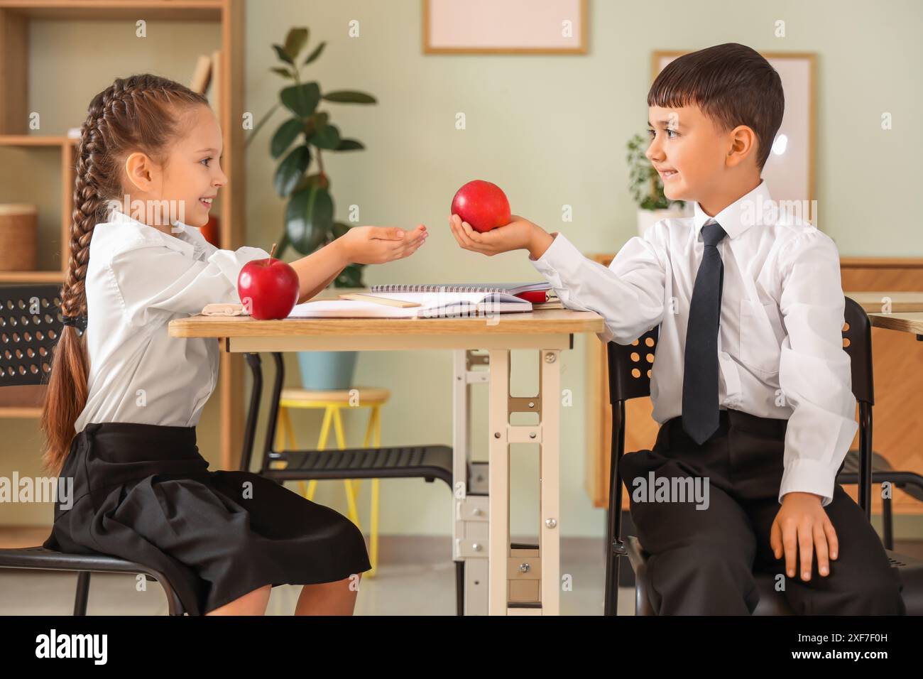 Little schoolgirl taking apple from classmate in classroom Stock Photo ...