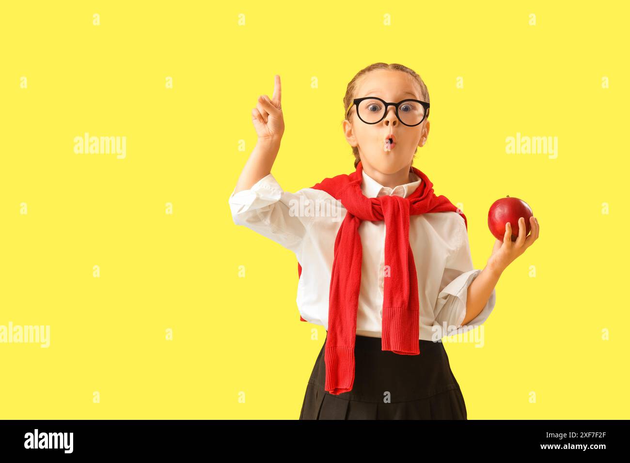 Little schoolgirl with apple pointing at something on yellow background ...