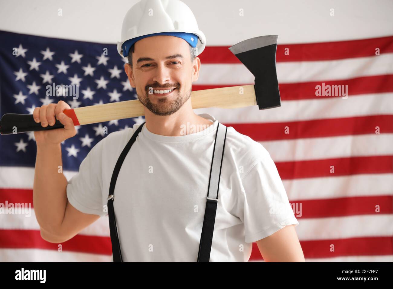Male firefighter with axe against USA flag on light background. Labour ...