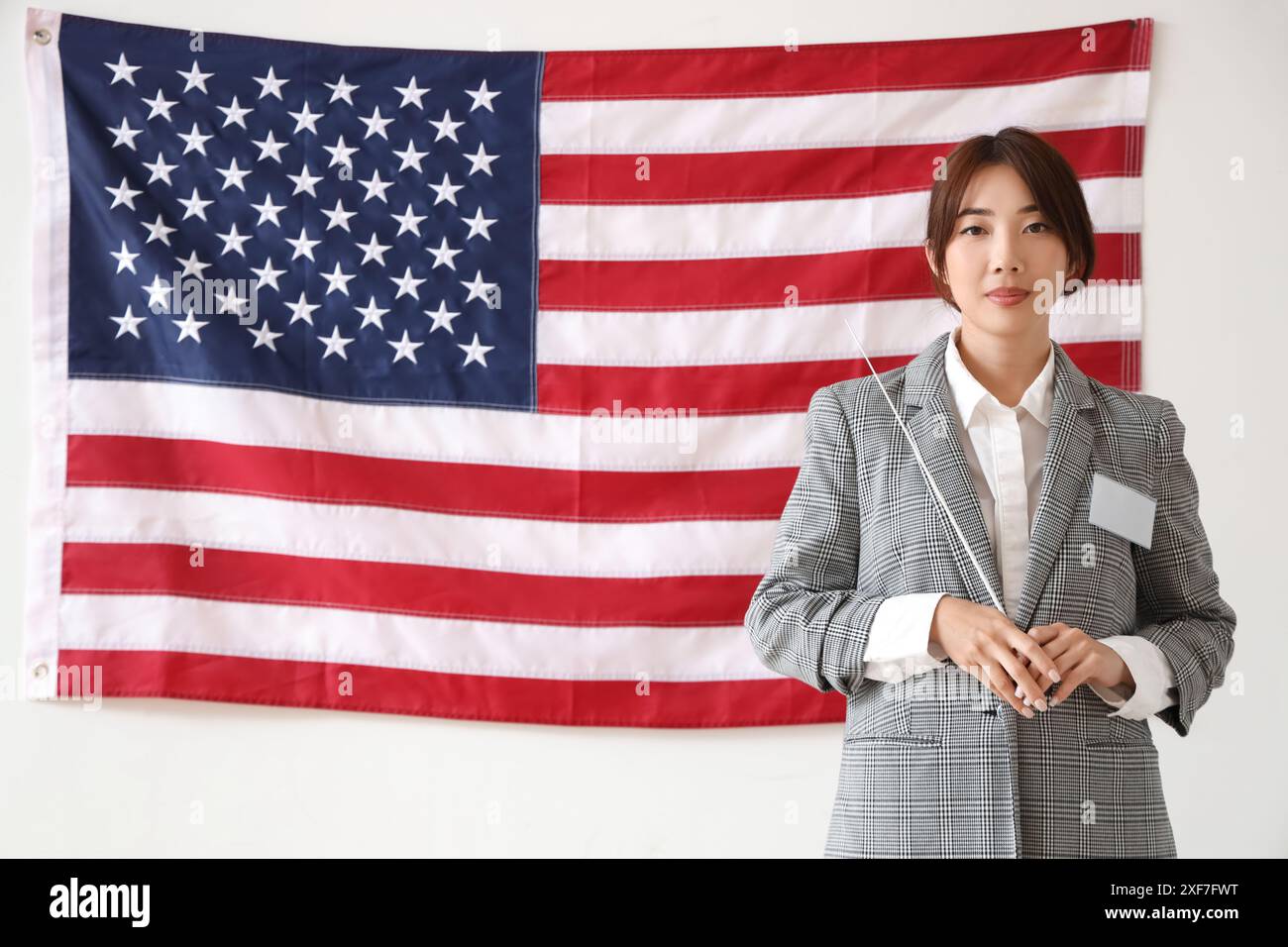 Female Asian teacher with pointer against USA flag on light background ...