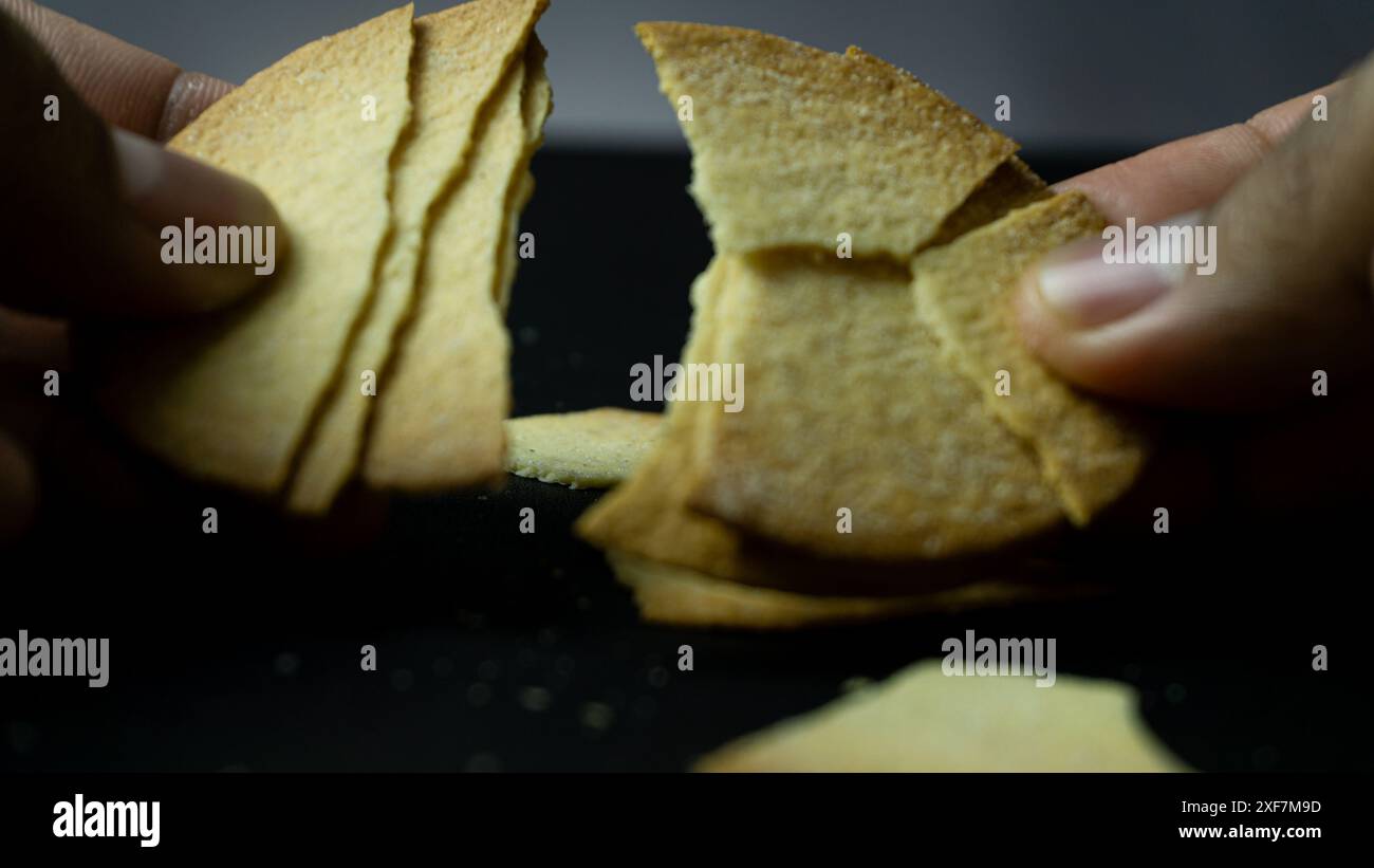 Baked chips being broken by hand on a black background table Stock ...