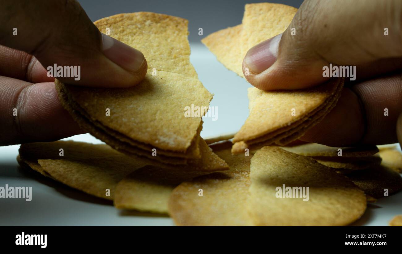 Baked chips being broken by hand on a white background table Stock ...