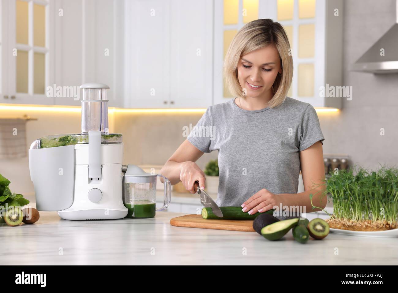 Juicer and fresh products on white marble table. Smiling woman cutting ...