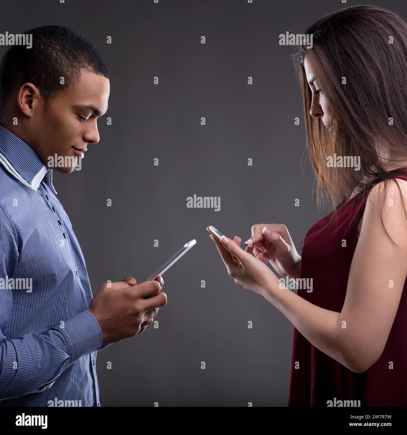 Young couple standing together, absorbed in smartphones, showing the ...