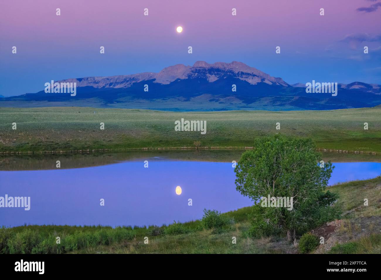 full moon setting over sawtooth ridge reflected in a prairie pond near ...