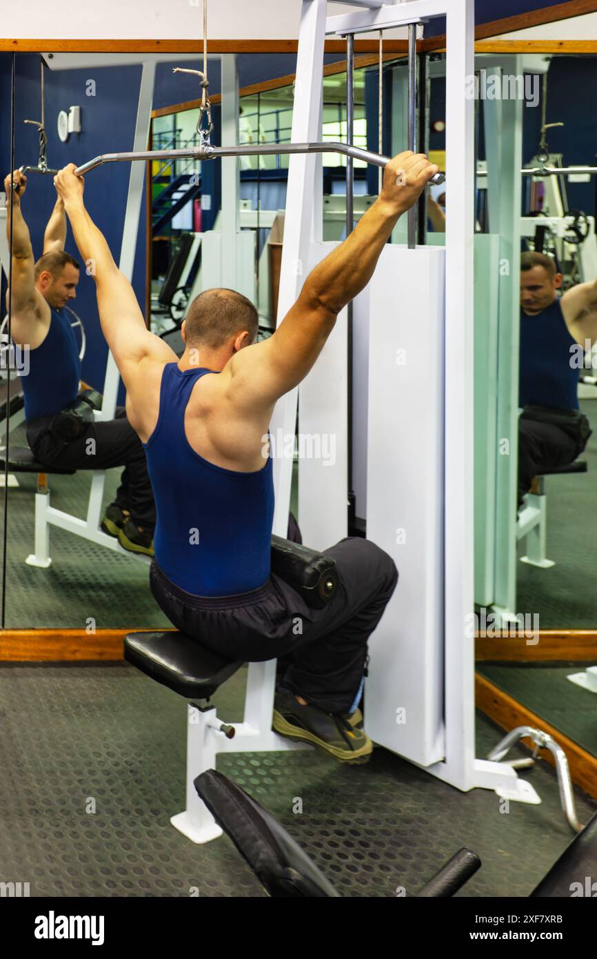man lifting weights at the gym in a machine , back exercise pulling ...