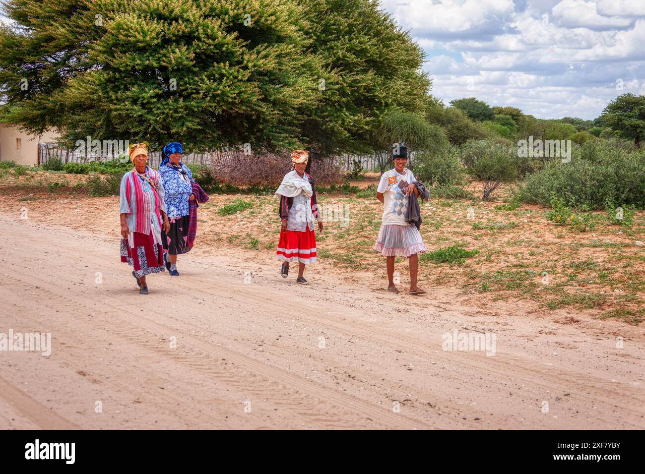 Basarwa african women walking on dirt road out of the village, San ...
