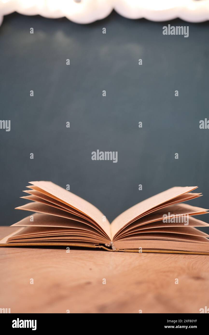 An open book with its pages gently turning rests on a wooden table in ...