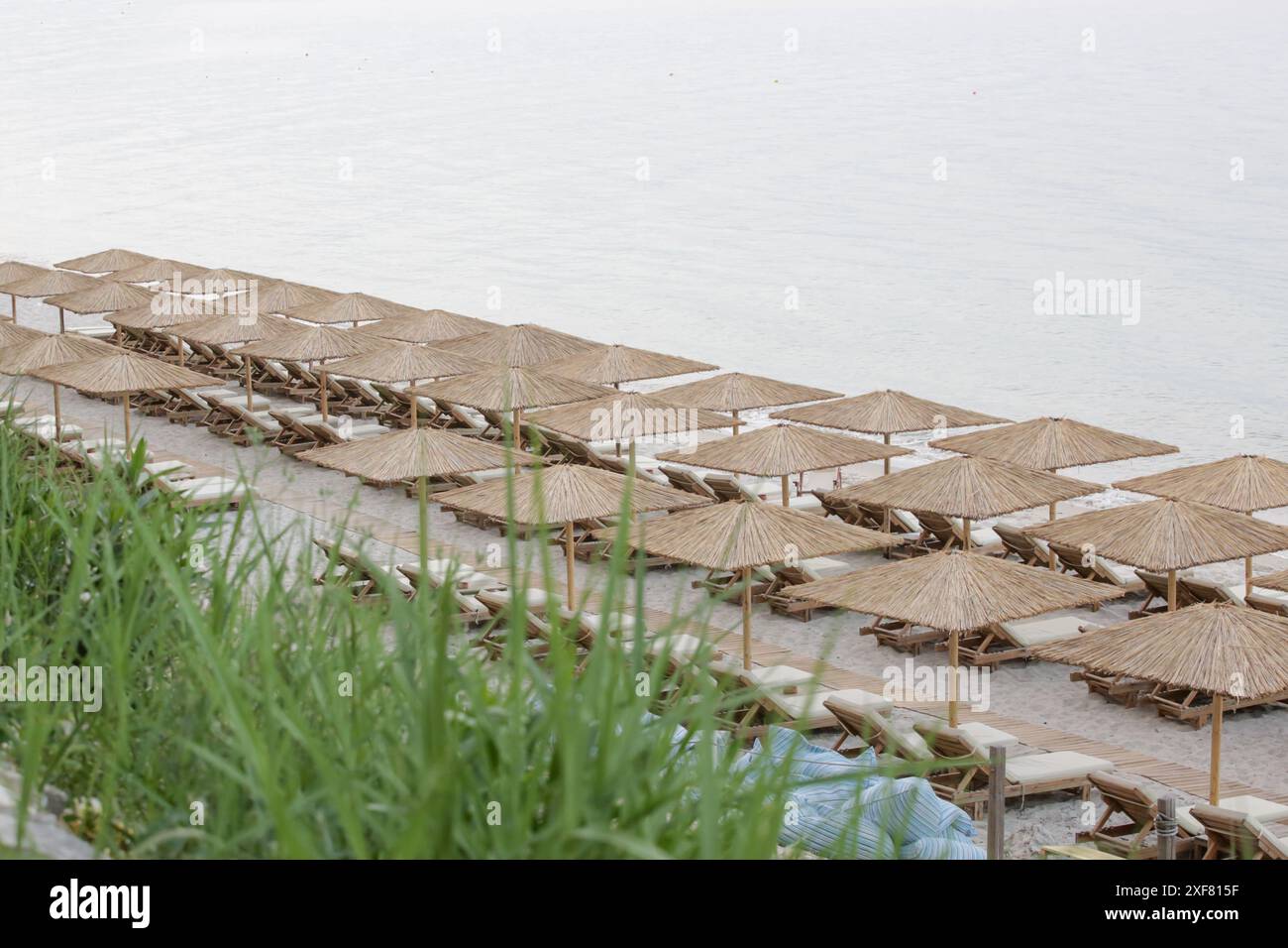 Empty beach with straw umbrellas and wooden sunbeds Stock Photo - Alamy