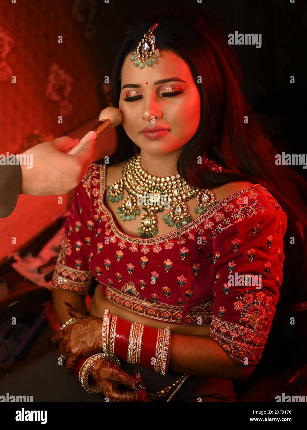 A young Indian bride getting makeup applied for a traditional Indian ...