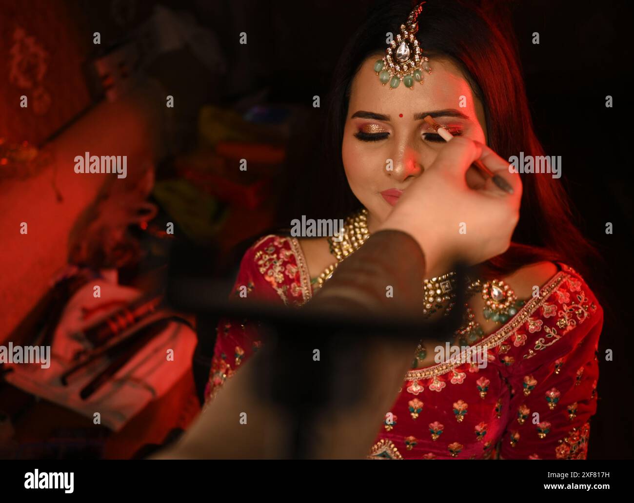 A young Indian bride getting makeup applied for a traditional Indian ...