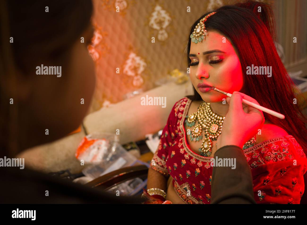 A young Indian bride getting makeup applied for a traditional Indian ...