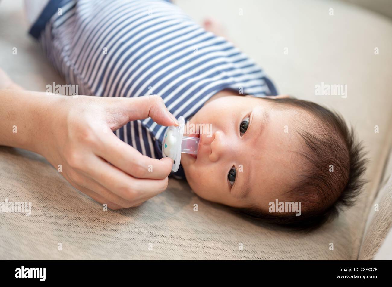 A close-up image of a mom putting a baby pacifier to her infant son. An ...