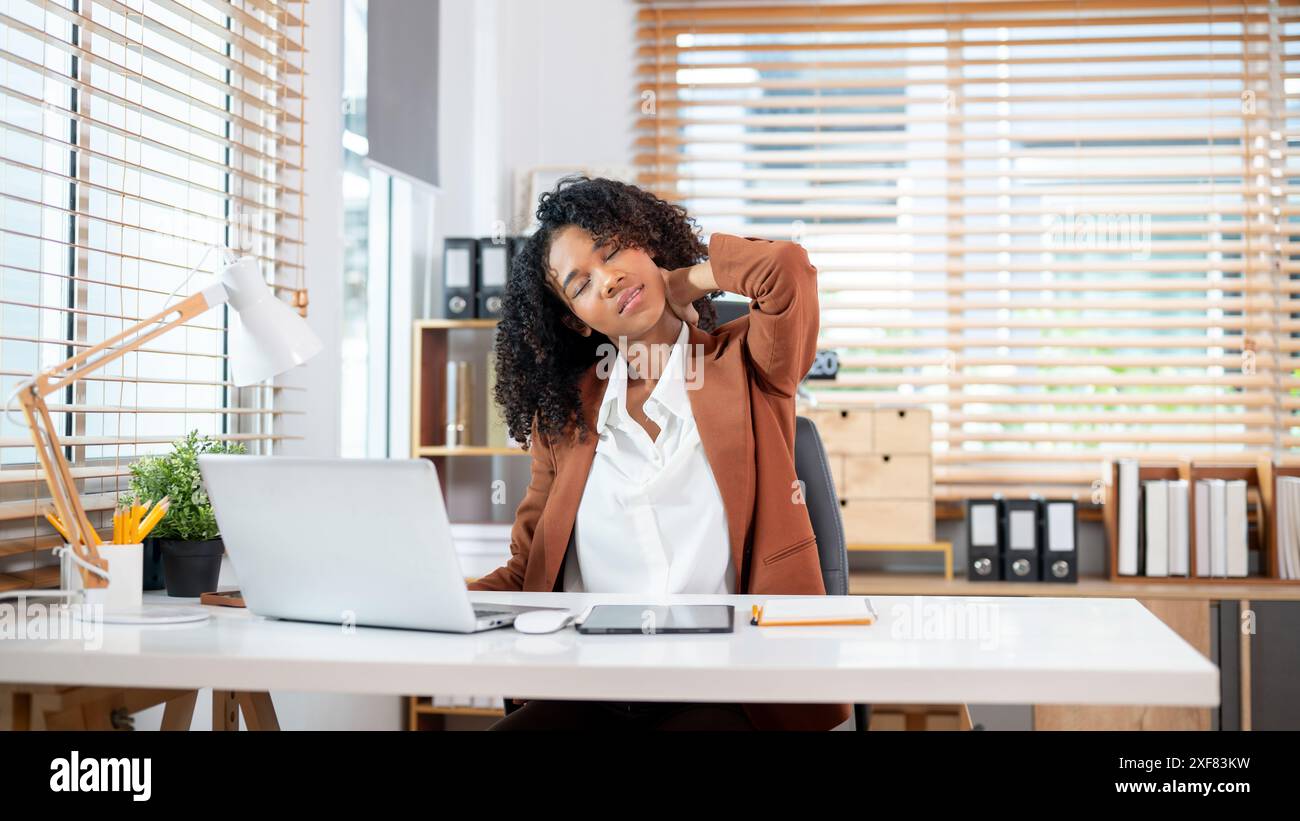 A tired, overworked Black businesswoman is massaging her neck ...