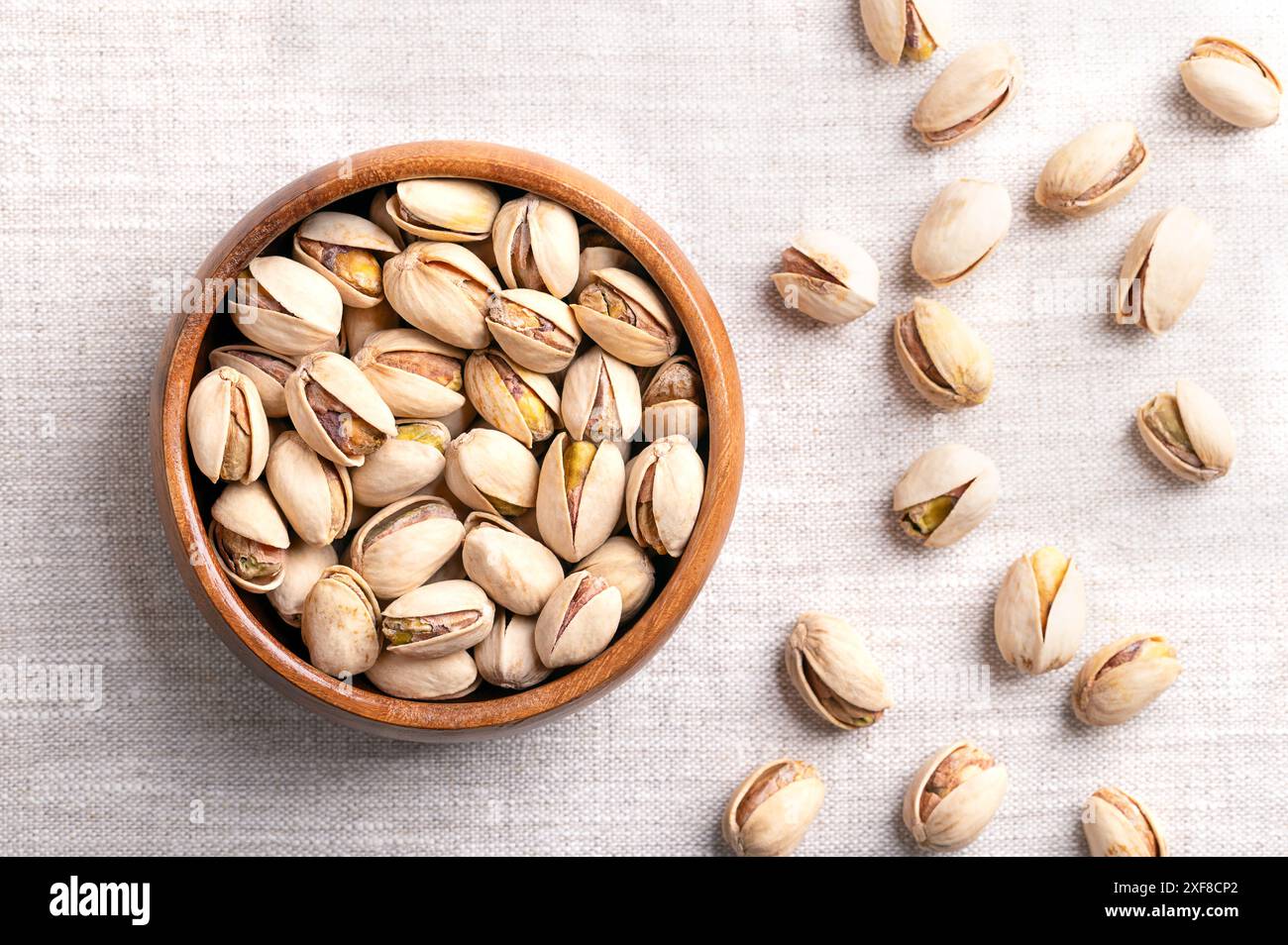 Pistachios in their shells, roasted and salted, in wooden bowl on linen. Crunchy roasted fruits ...