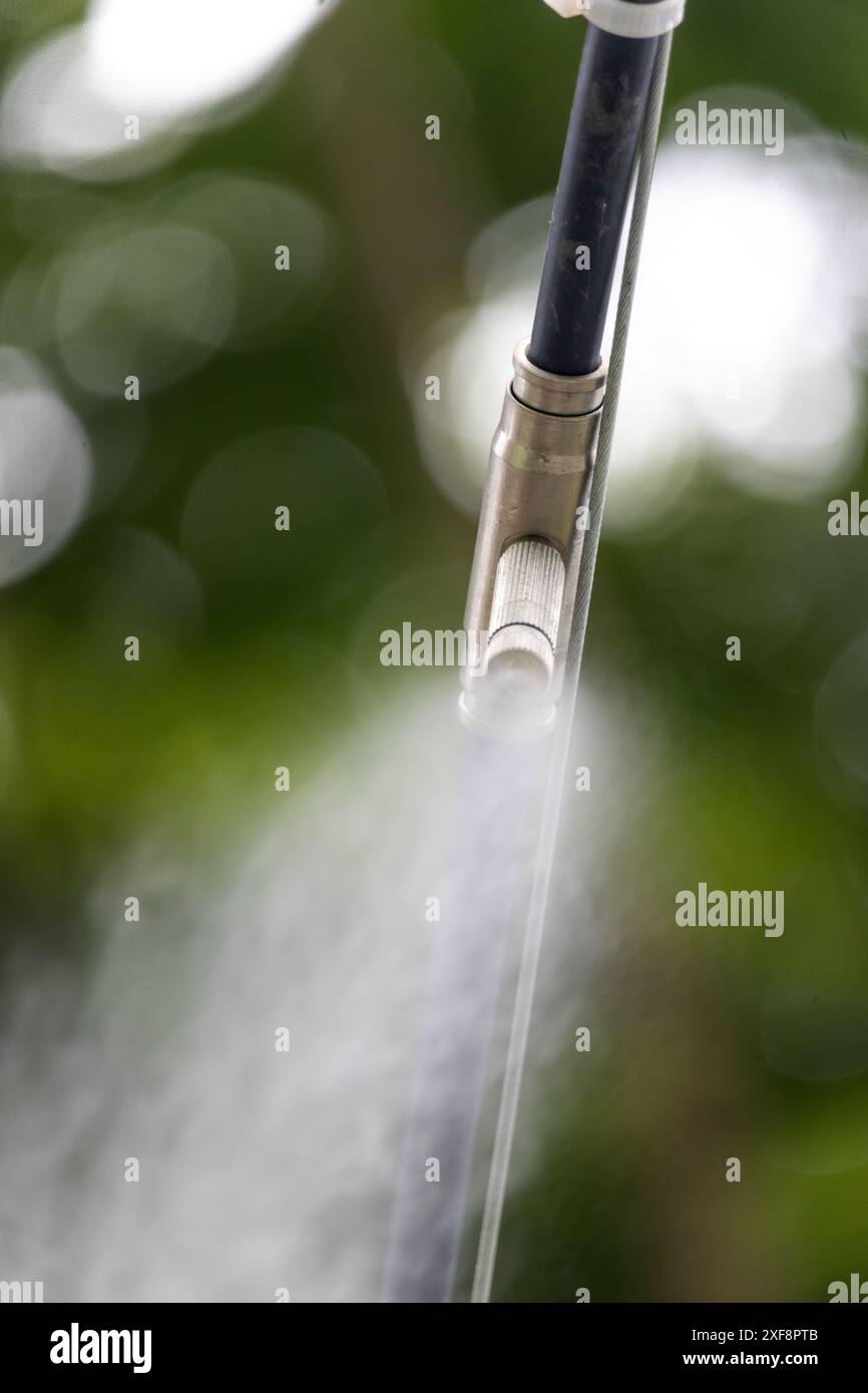 Water aerosol is jetting from a hanging hose in the park, close up ...