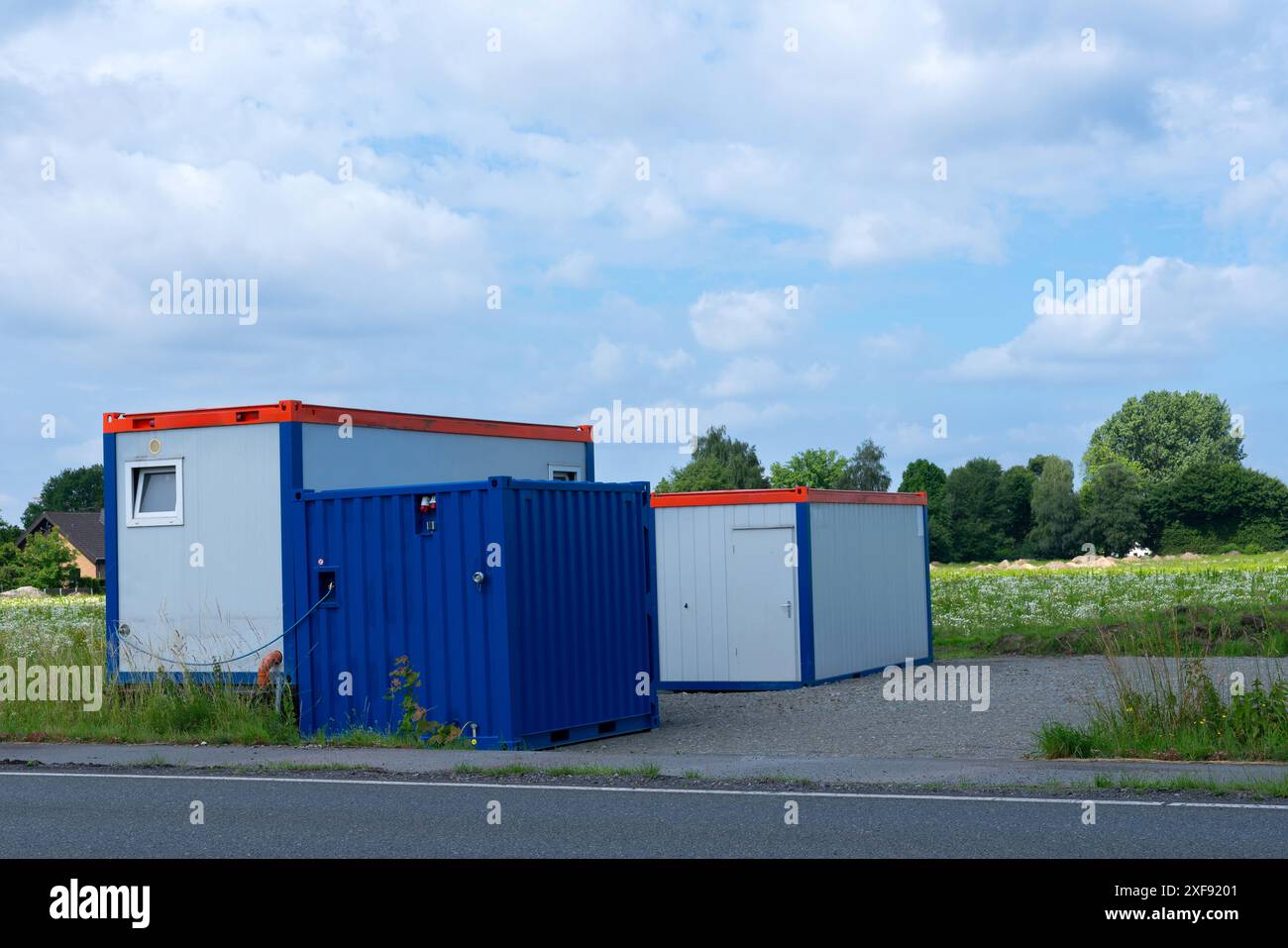 Three shipping containers sit side-by-side on a gravel lot. The sky is ...