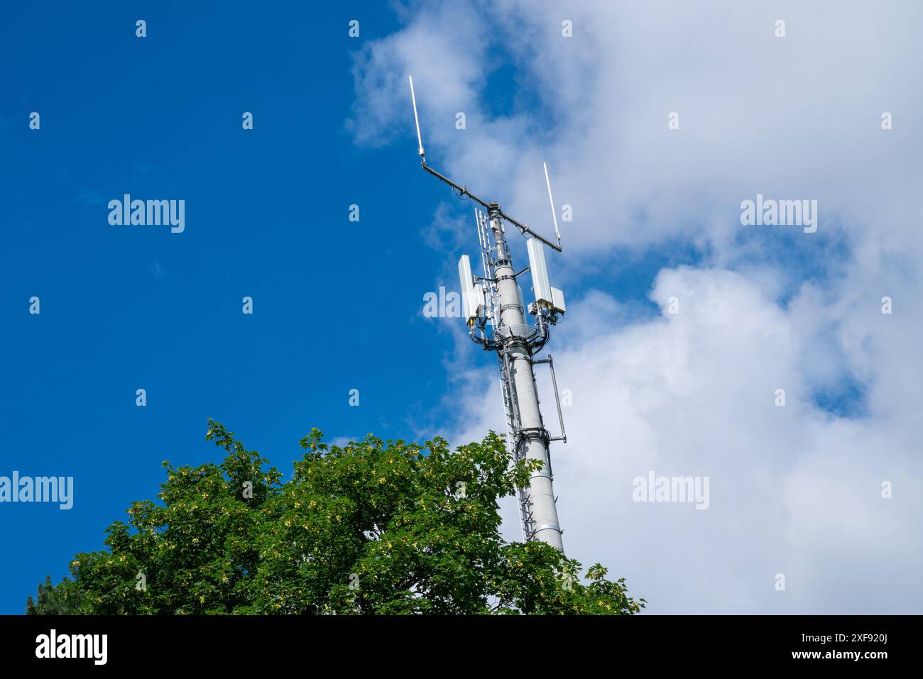 A tall cellular tower stands tall against a blue sky with white clouds Stock Photo - Alamy