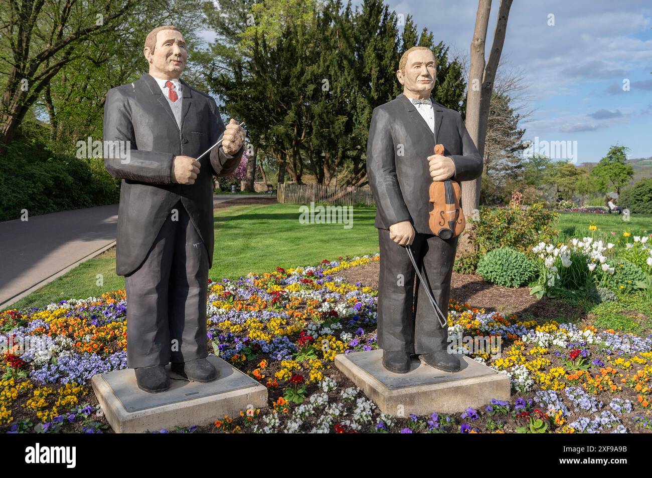 Two statues of men in classic suits stand side by side in a flowering ...
