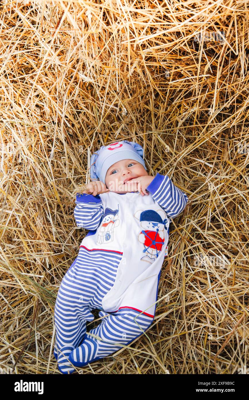 A baby dressed in a blue and white outfit with a hat lying on a bed of ...