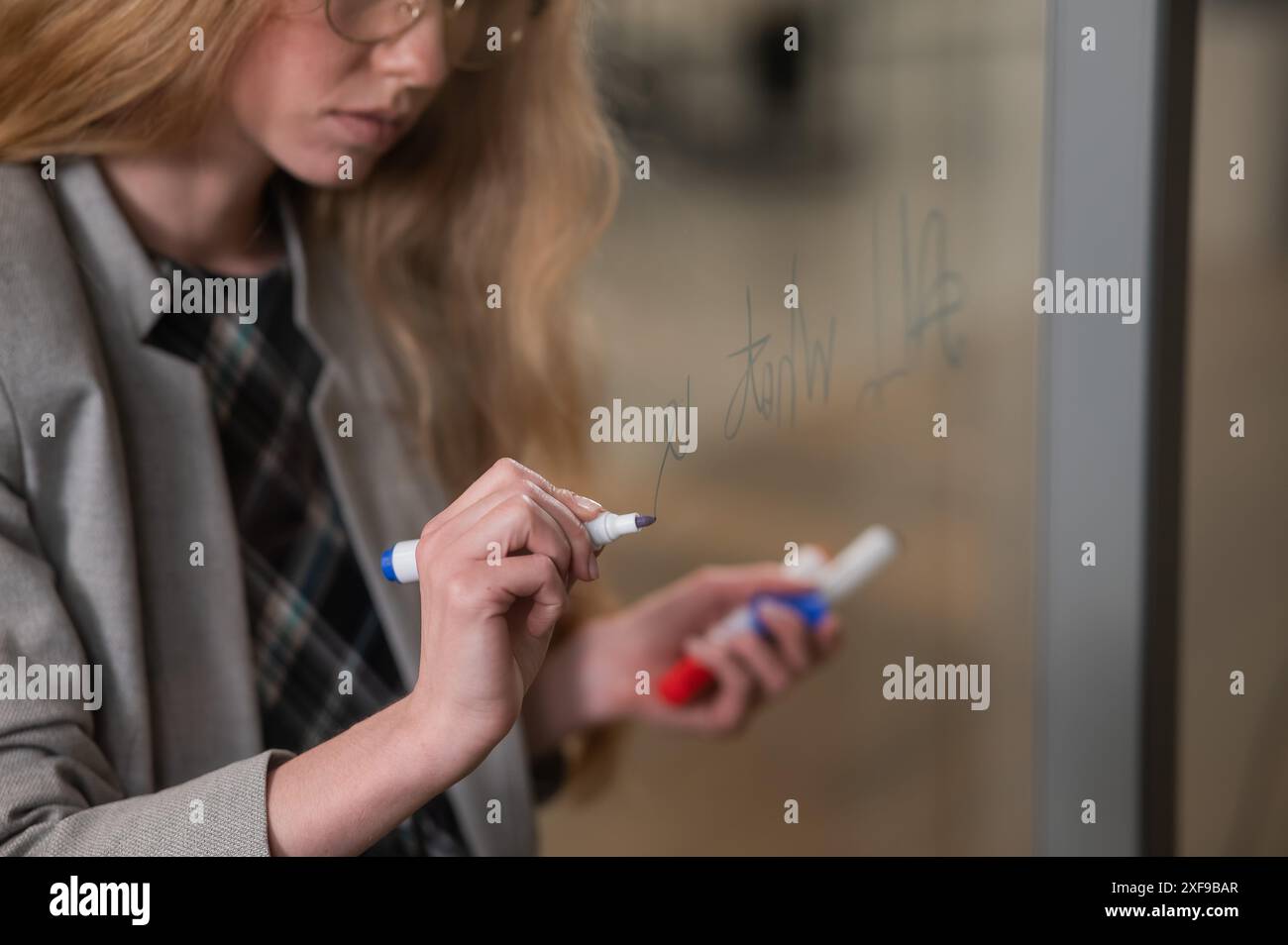 Caucasian woman with glasses writes text in English on a glass wall ...
