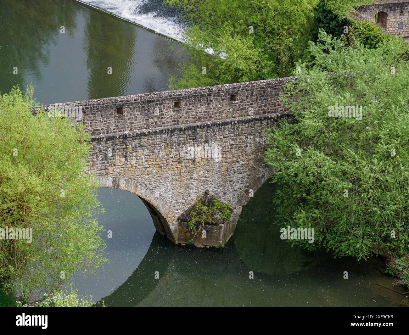 Stone bridge from the Middle Ages crossing a quiet river between green ...