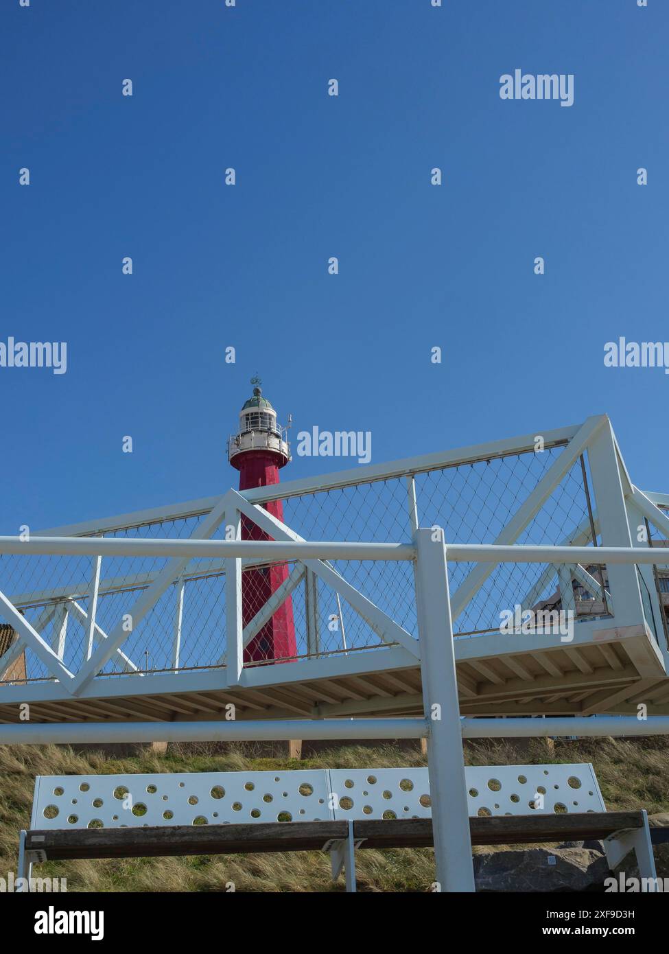Red lighthouse behind a white metal bridge under a blue sky ...