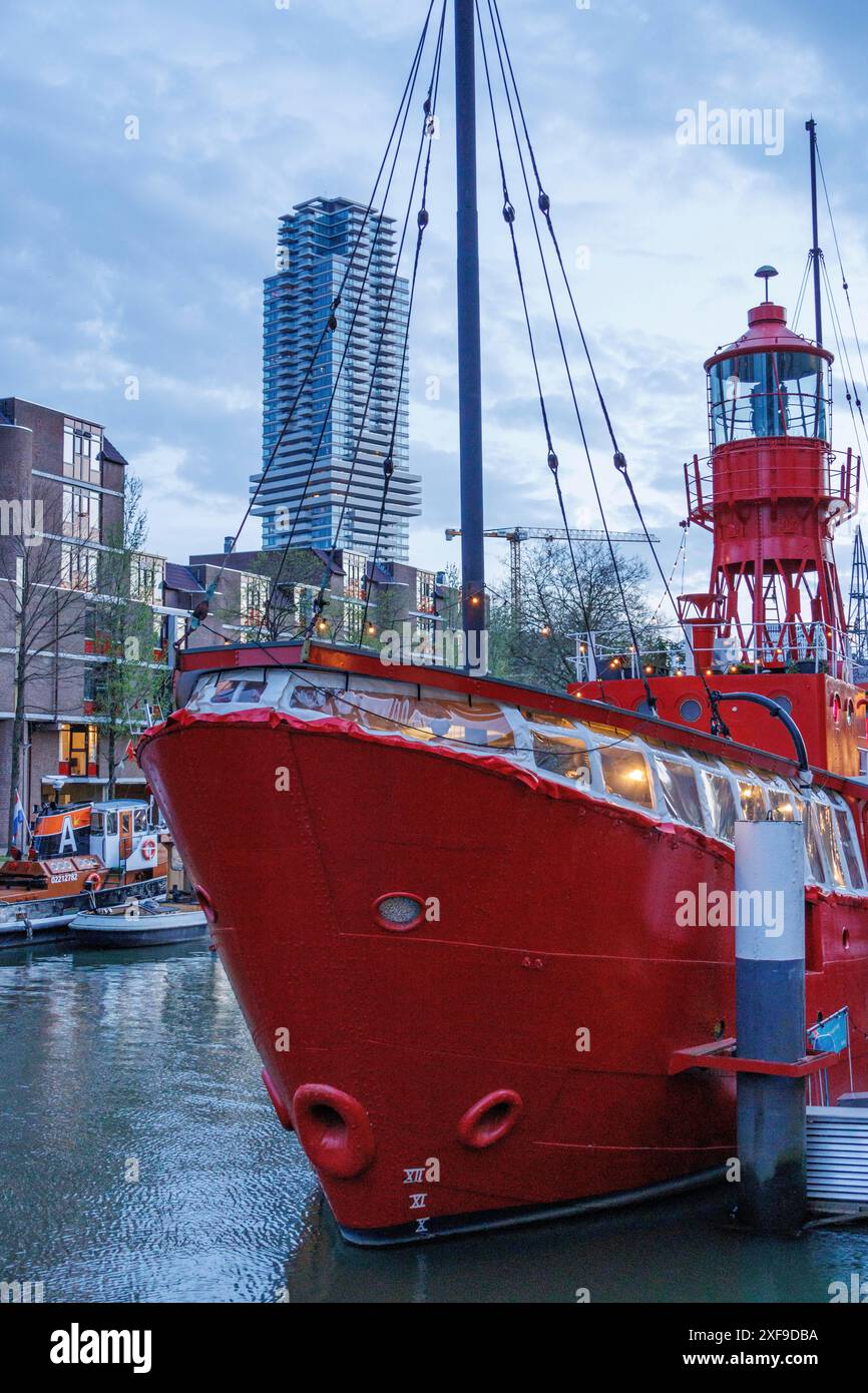 A red lighthouse ship in the water under modern high-rise buildings in ...