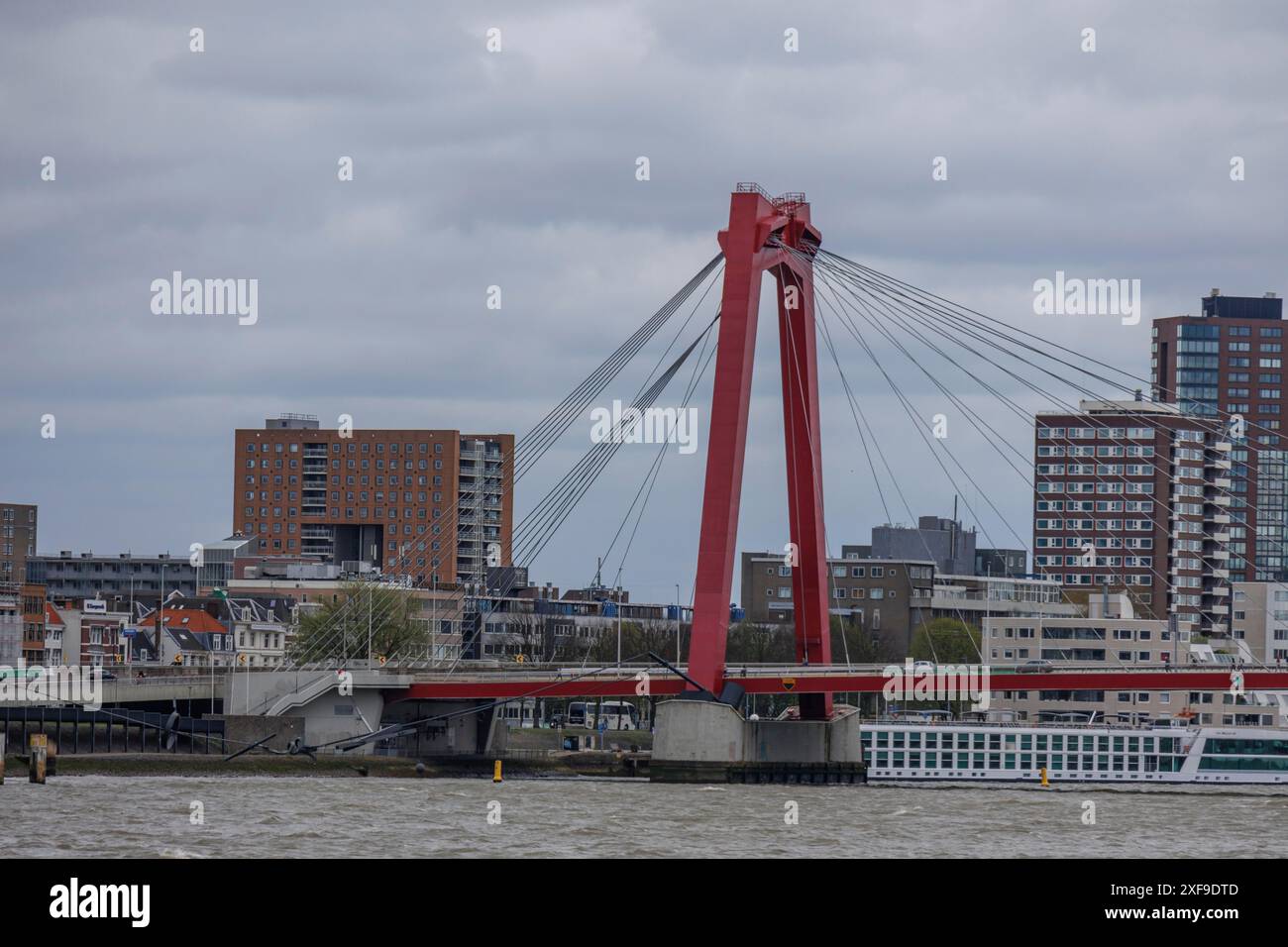 Red suspension bridge over a river in Rotterdam, surrounded by modern ...