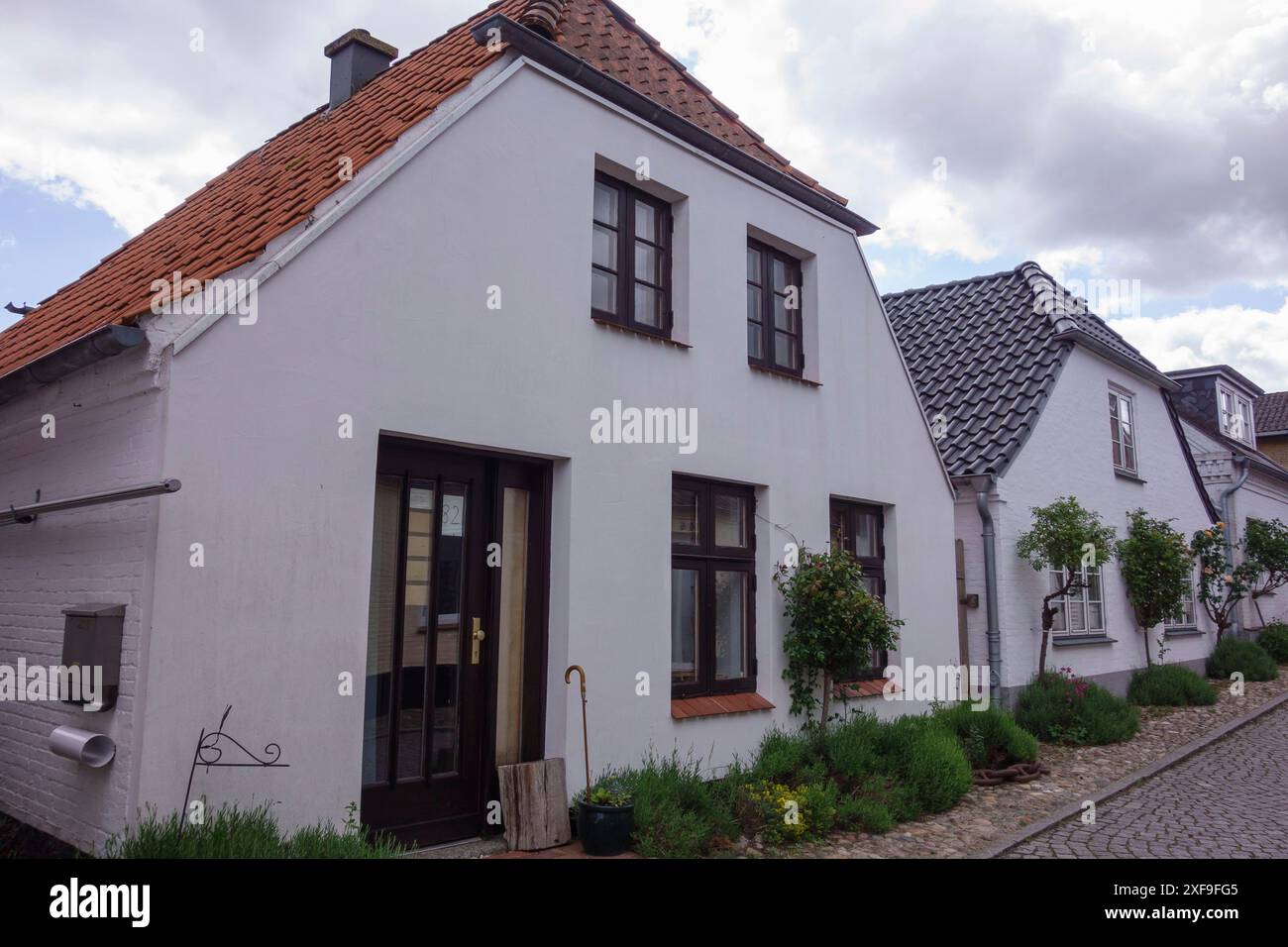 White house with dark red roof, windows and doors along a narrow street ...