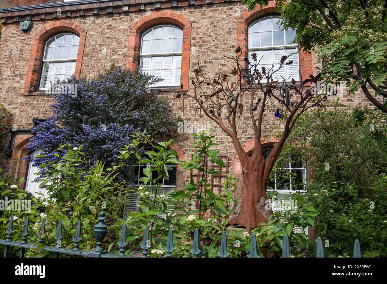 A red brick house facade with windows and a garden with various plants ...