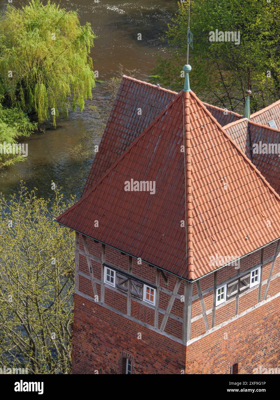 Brick tower with red tiled roof next to a river and green trees in ...
