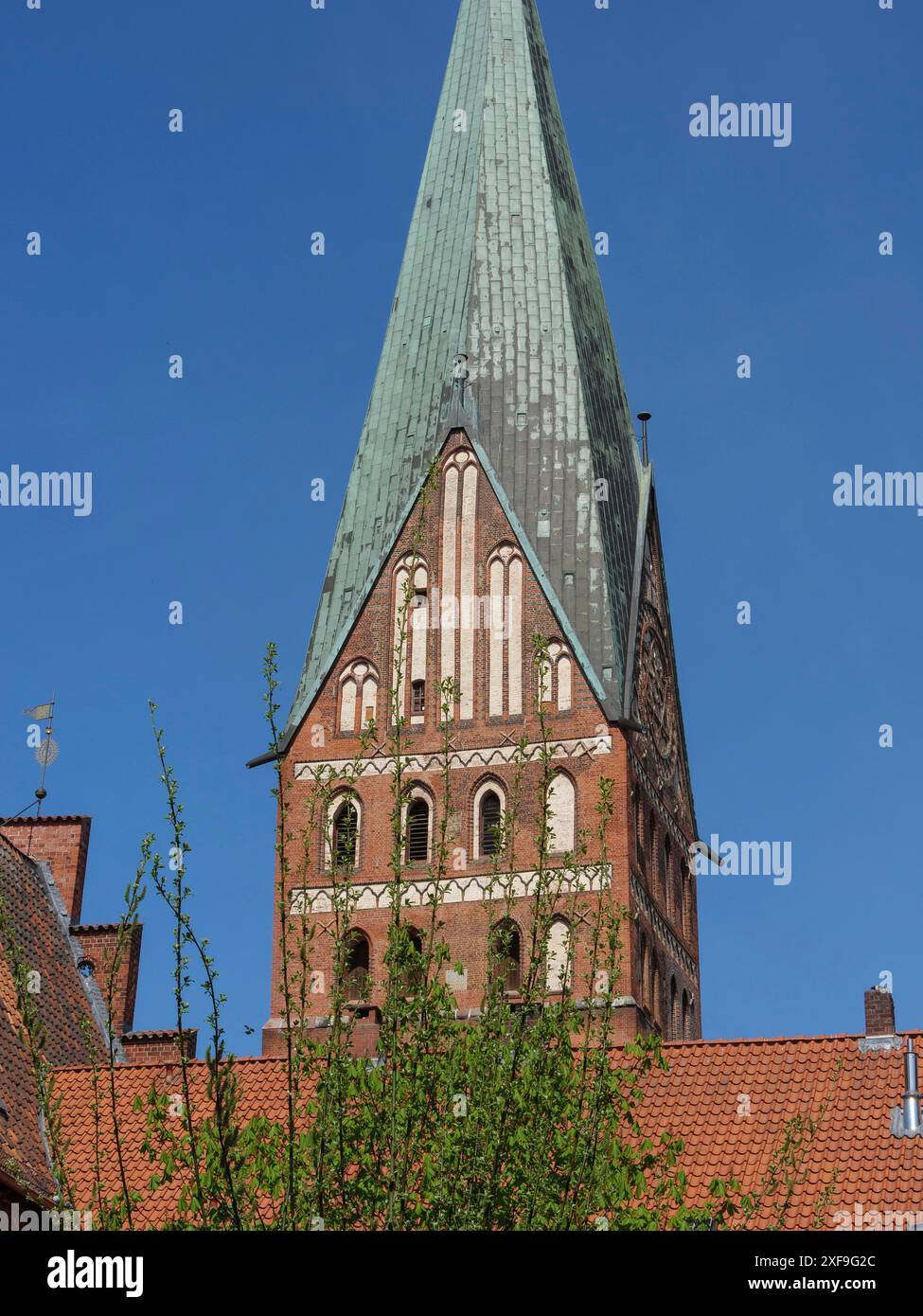 Pointed brick church tower towers above red roofs and green trees under ...