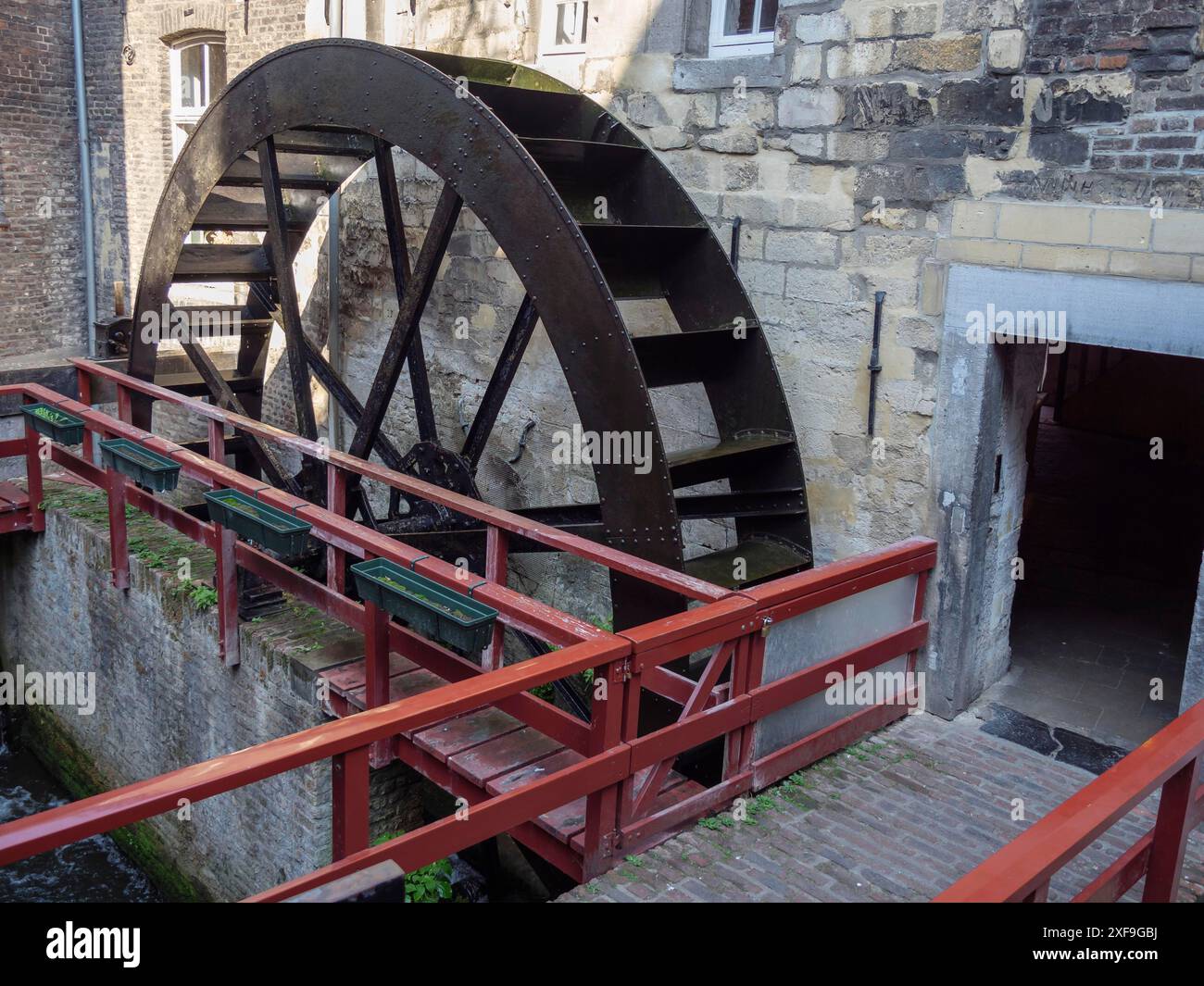 Watermill with a large mill wheel, red railings and a historic brick ...