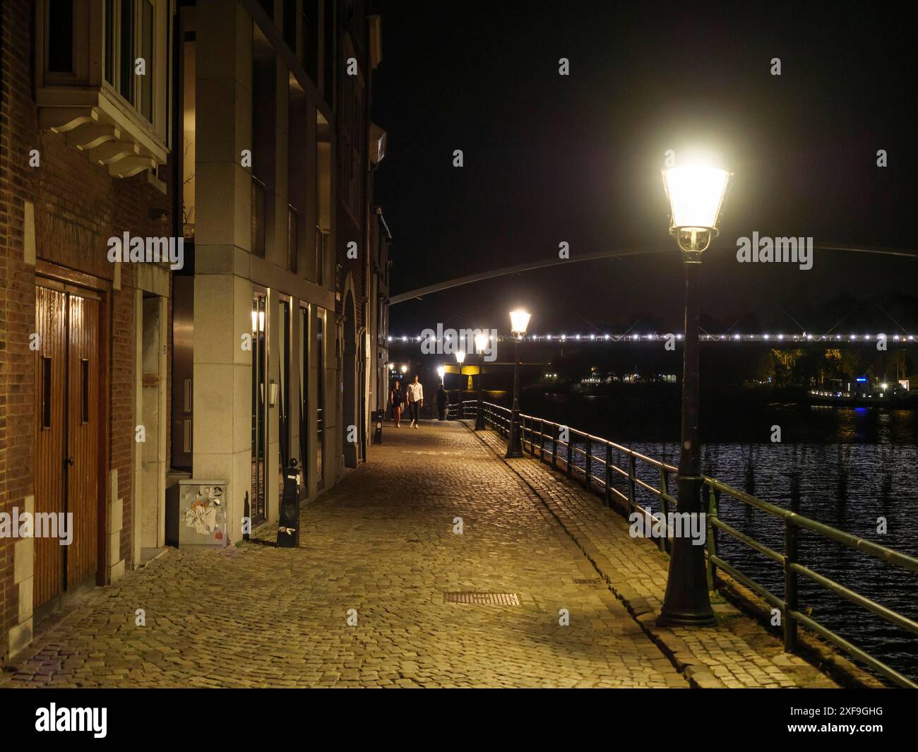 Empty, cobbled path on the riverbank illuminated by streetlights ...