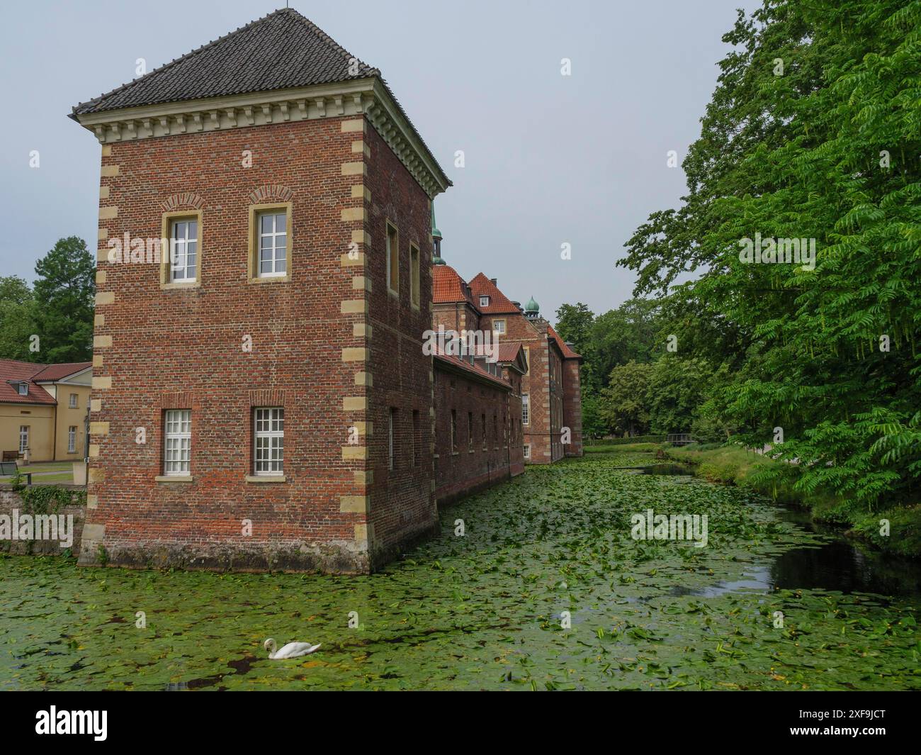 Historic brick castle with towers and moat, surrounded by green trees ...