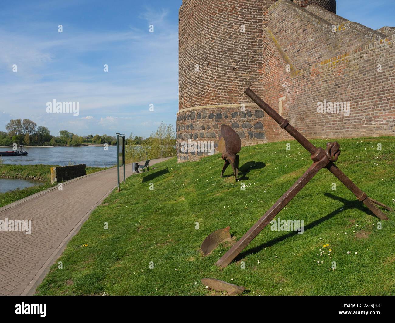 Iron anchor in front of a brick tower on a path along a river under a ...