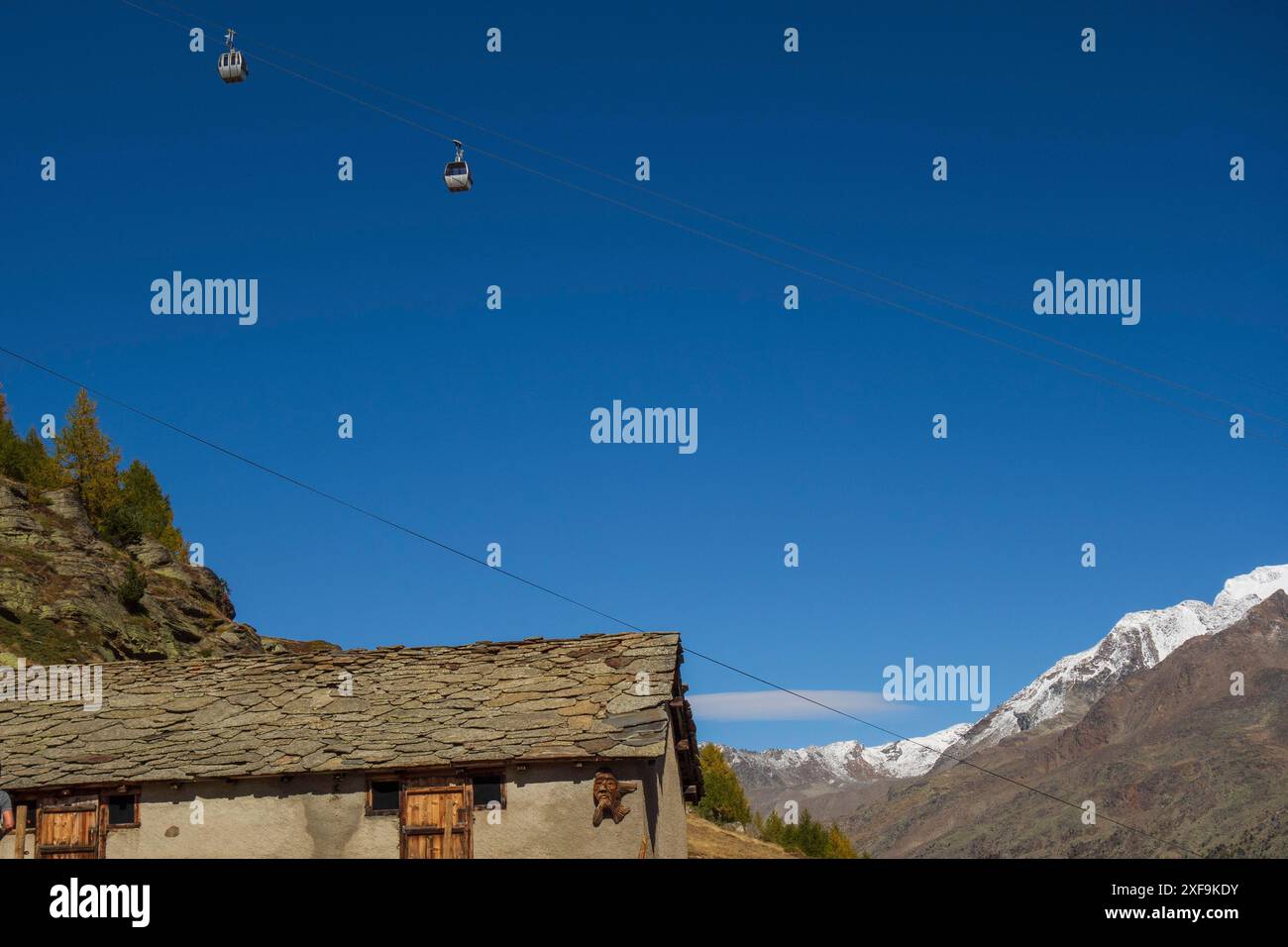 Cable cars hovering over a mountain hut with a clear blue sky and rocky ...