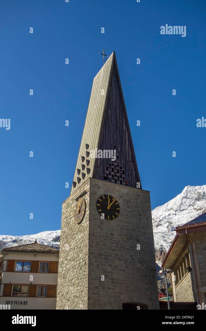 Modern church tower with clock and pointed roof against a blue sky ...