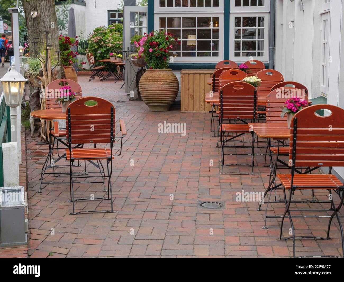 A cosy outdoor cafe area with red wooden chairs, tables and flower pots ...