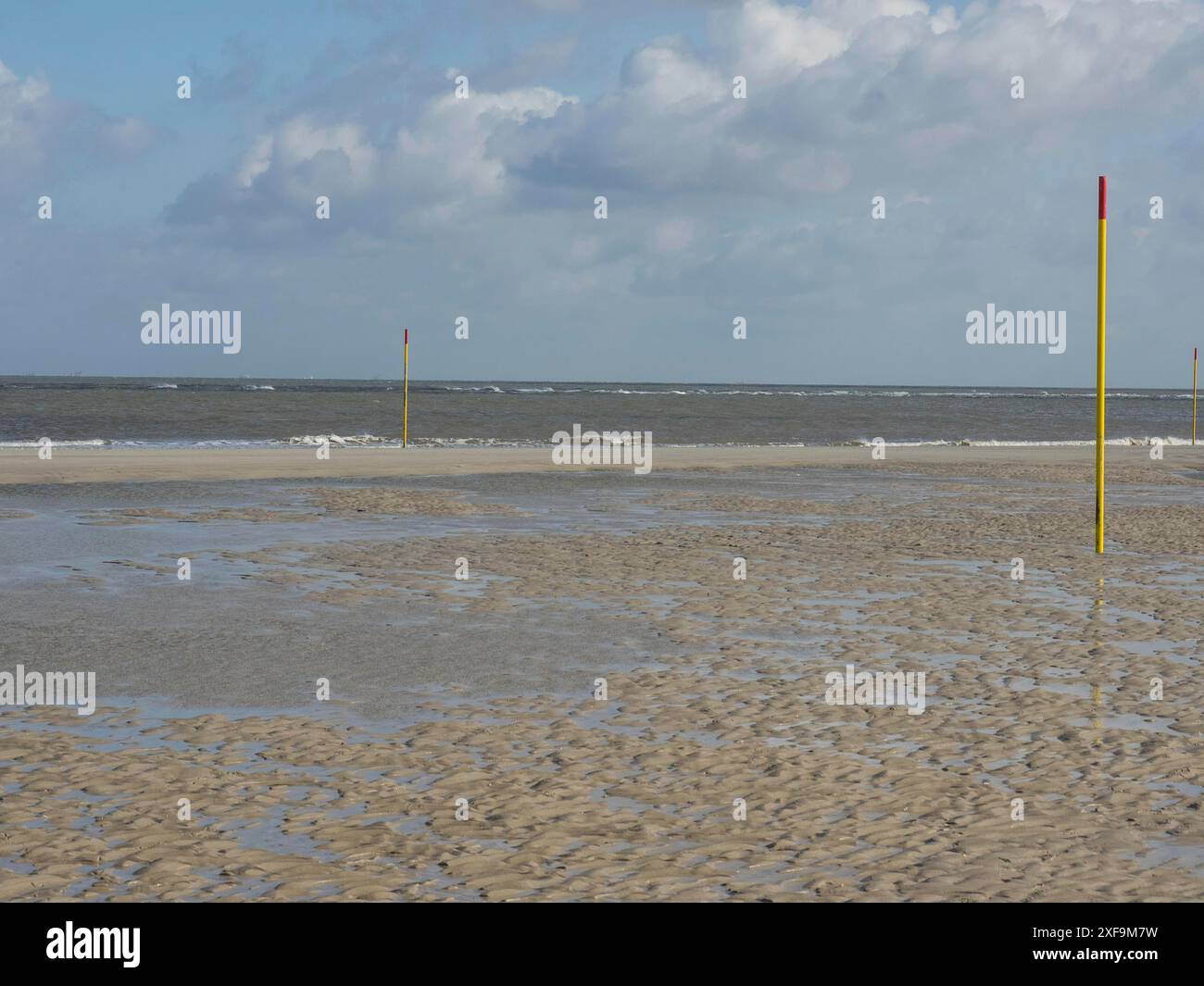 On the beach at low tide with visible silt, two yellow poles and a ...