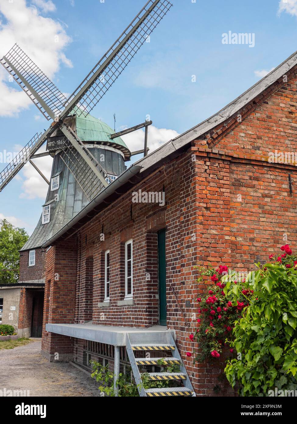 Brick windmill under a blue sky with white clouds and plants in the ...