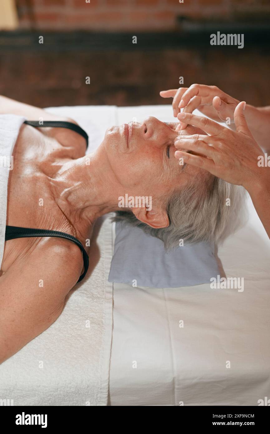 Beautician is giving a facial massage to a senior woman in a spa center ...