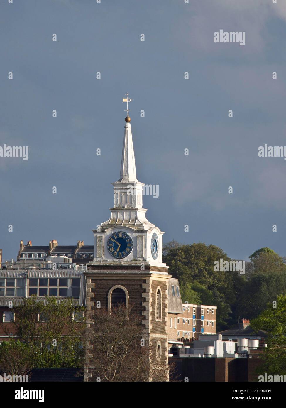 A bright church tower with clock in front of buildings and cloudy sky ...