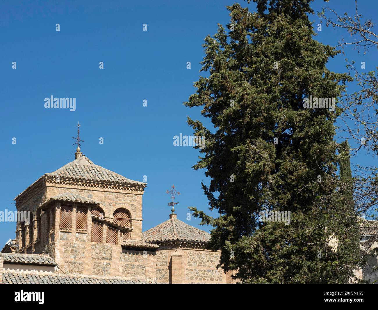 Stone building with towers and weather vanes surrounded by green trees ...