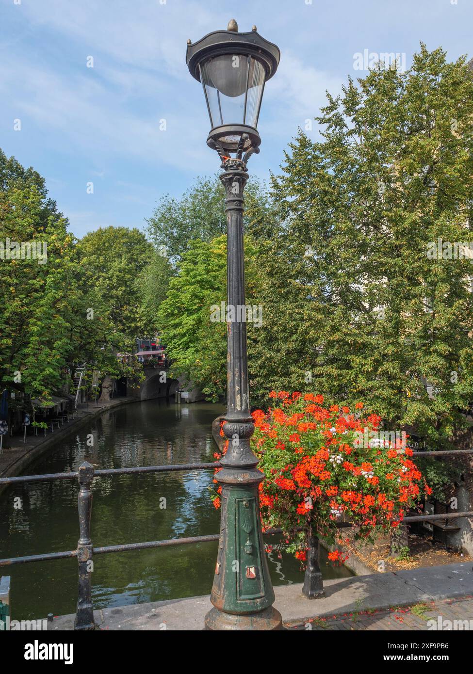 Romantic scene with an old lamppost, red flowers and a river surrounded ...