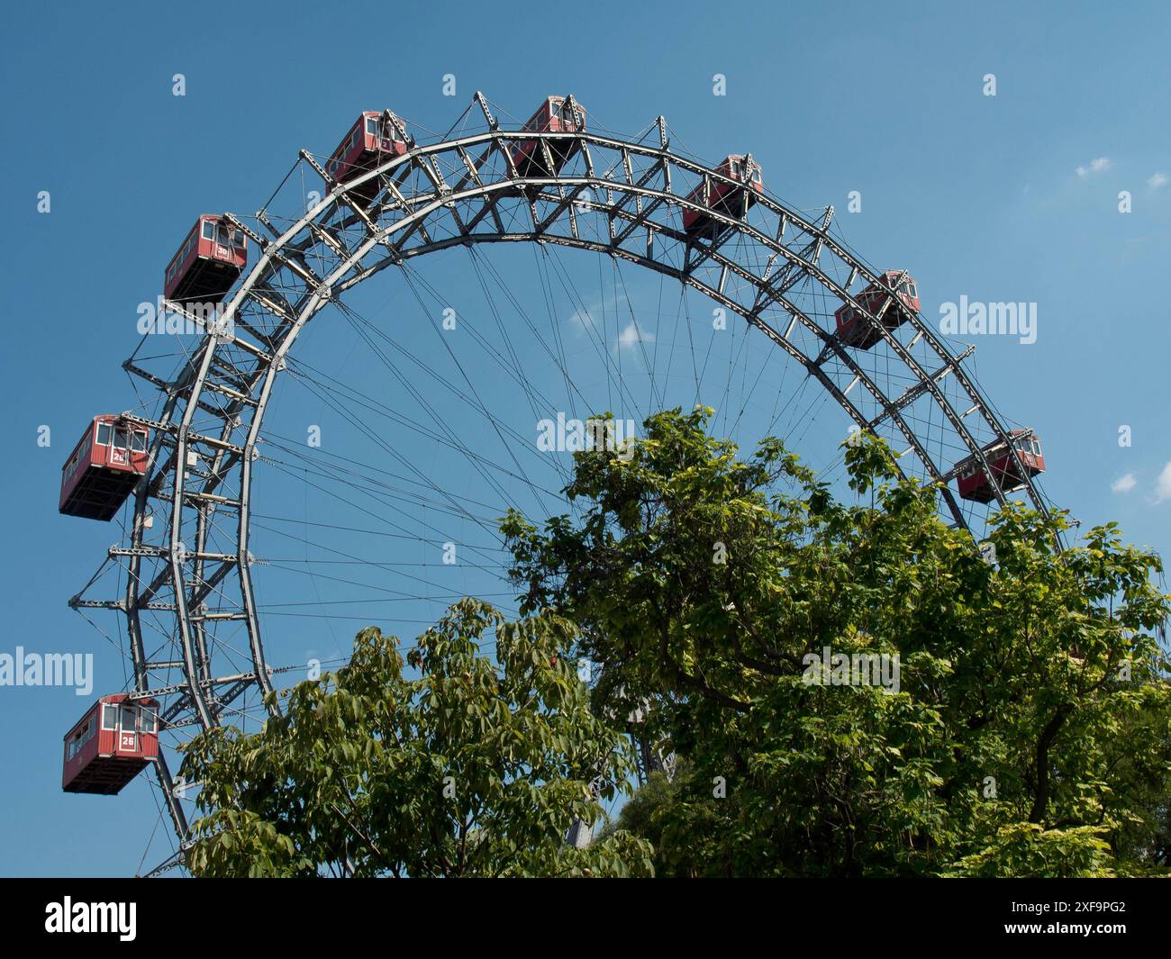 Large Ferris wheel with red cabins behind trees in an amusement park ...