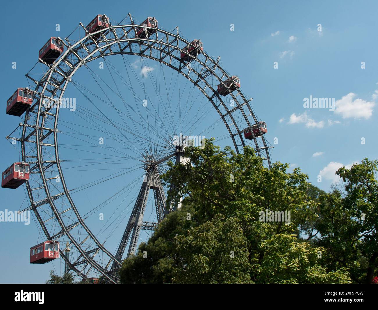 Large Ferris wheel with red cabins in front of green foliage and blue ...