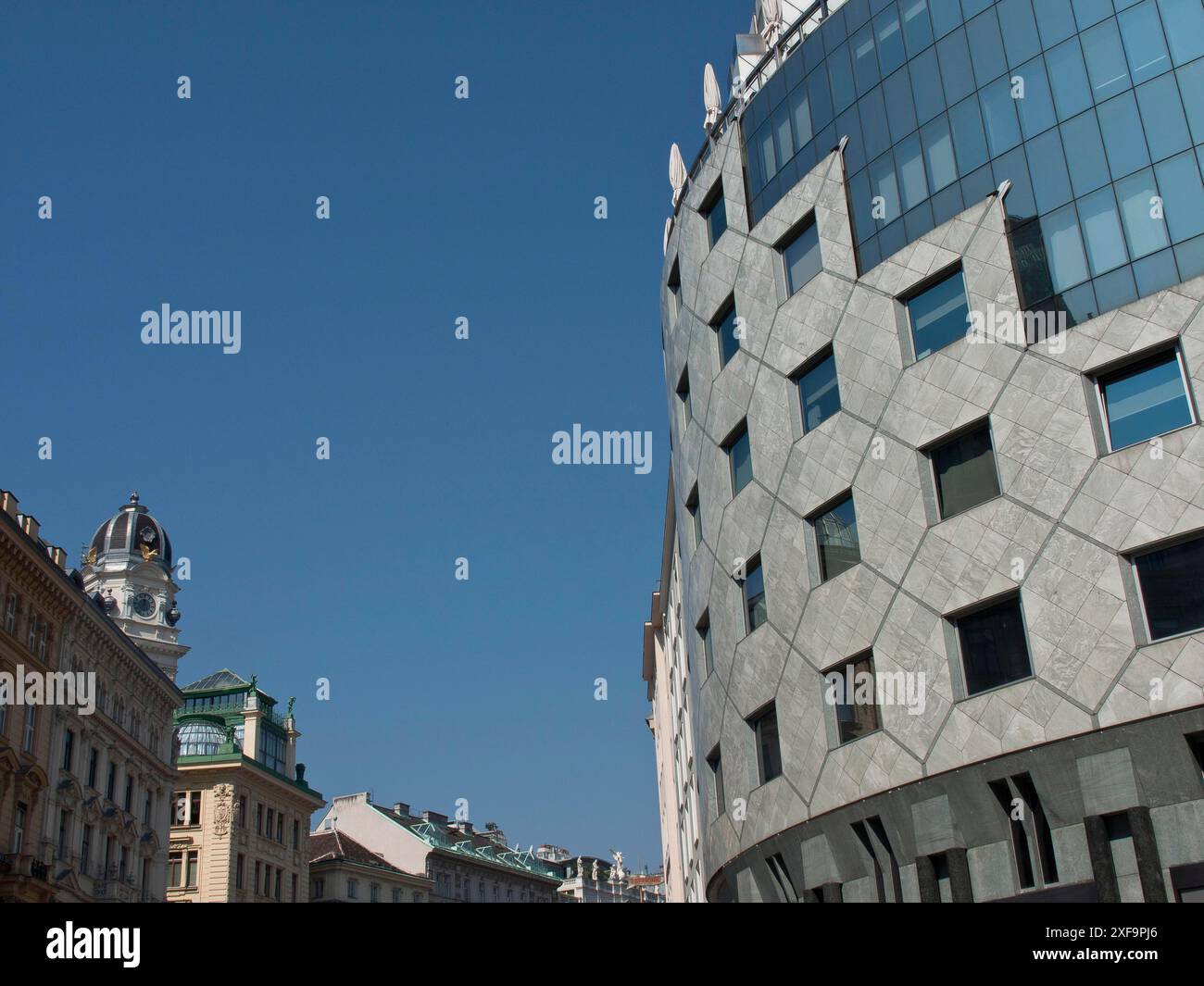 Modern glass facade with hexagonal structure next to historic buildings ...